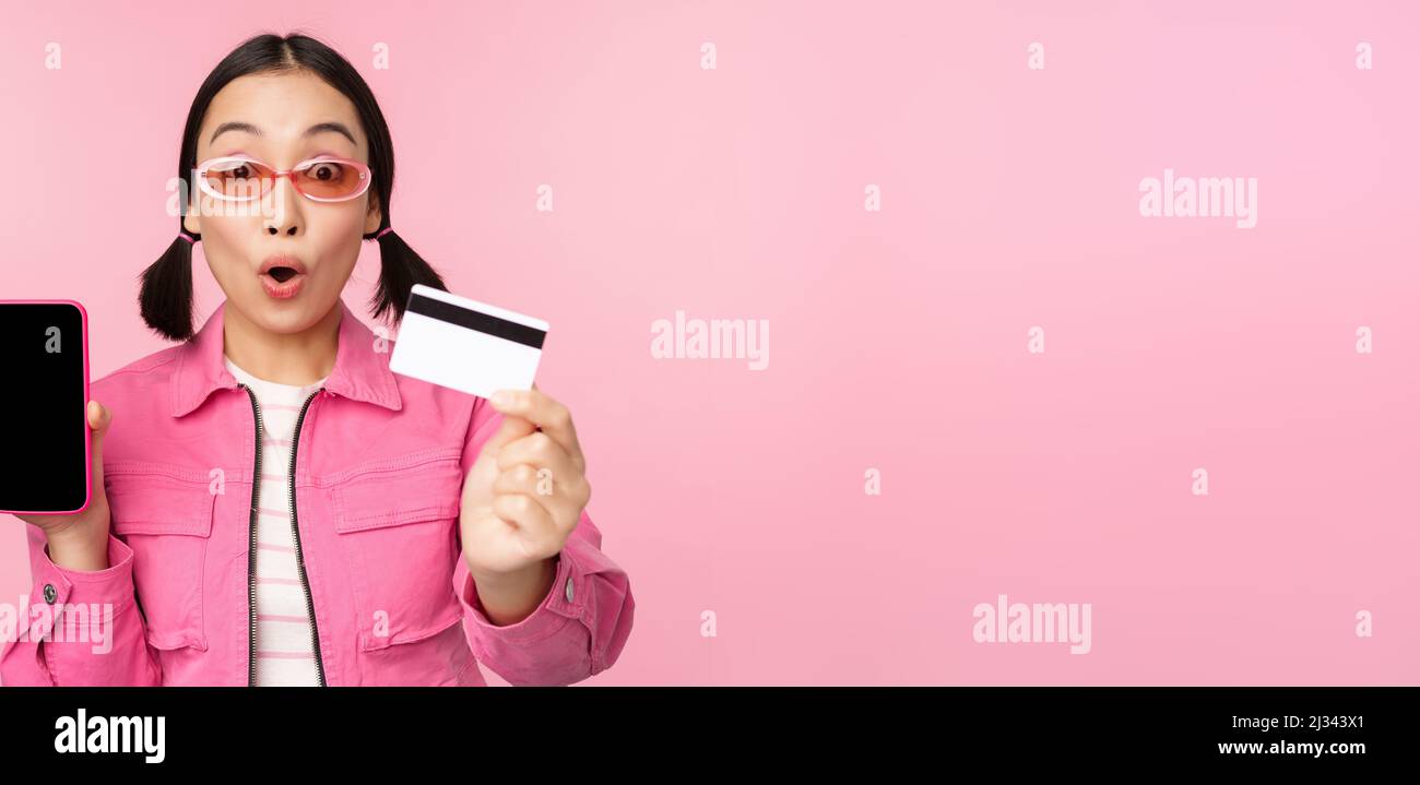 Asian girl shows mobile phone screen and credit card, reacts surprised ...
