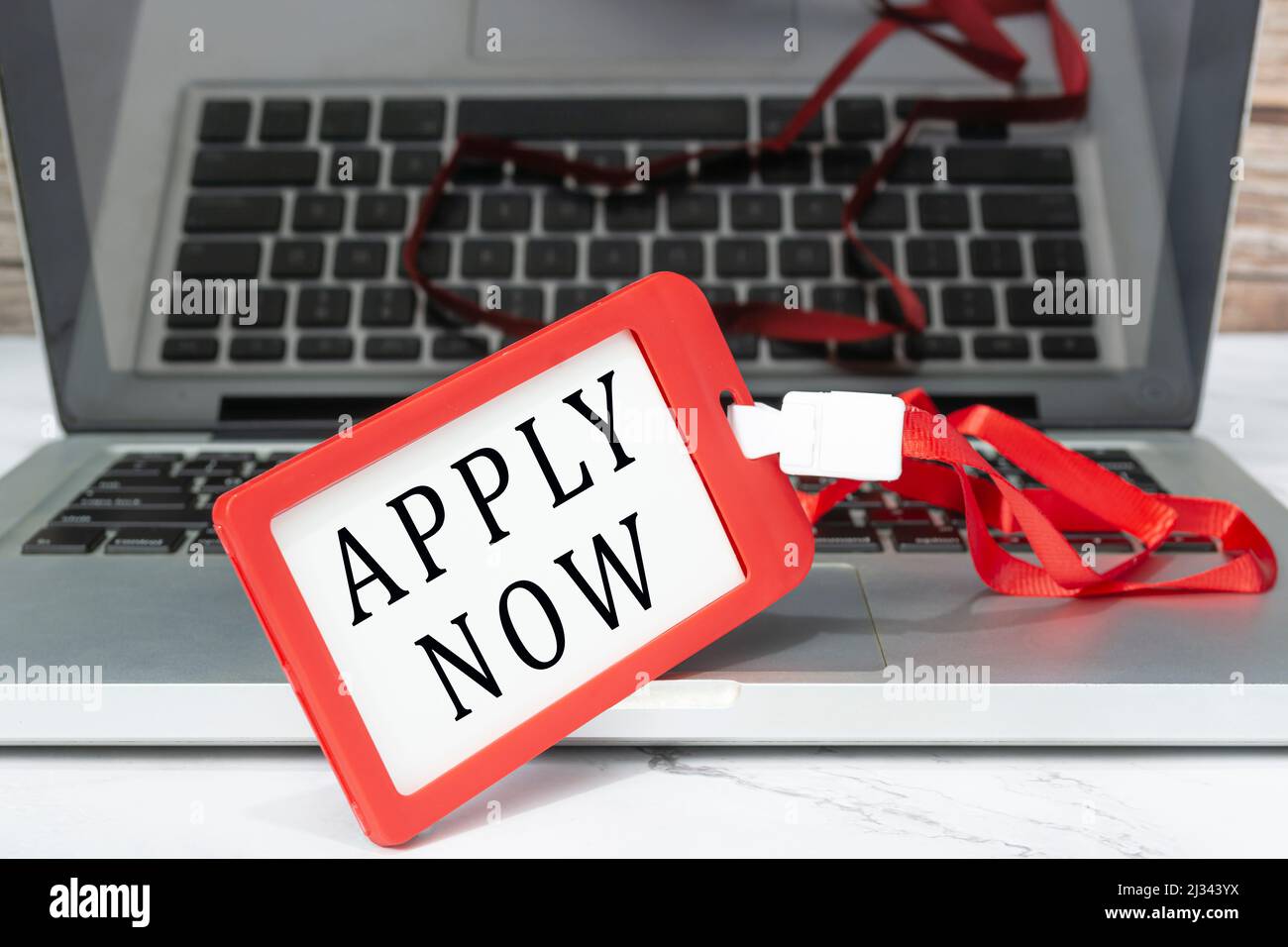 Apply now text written on red name tag placed on a laptop or notebook ...