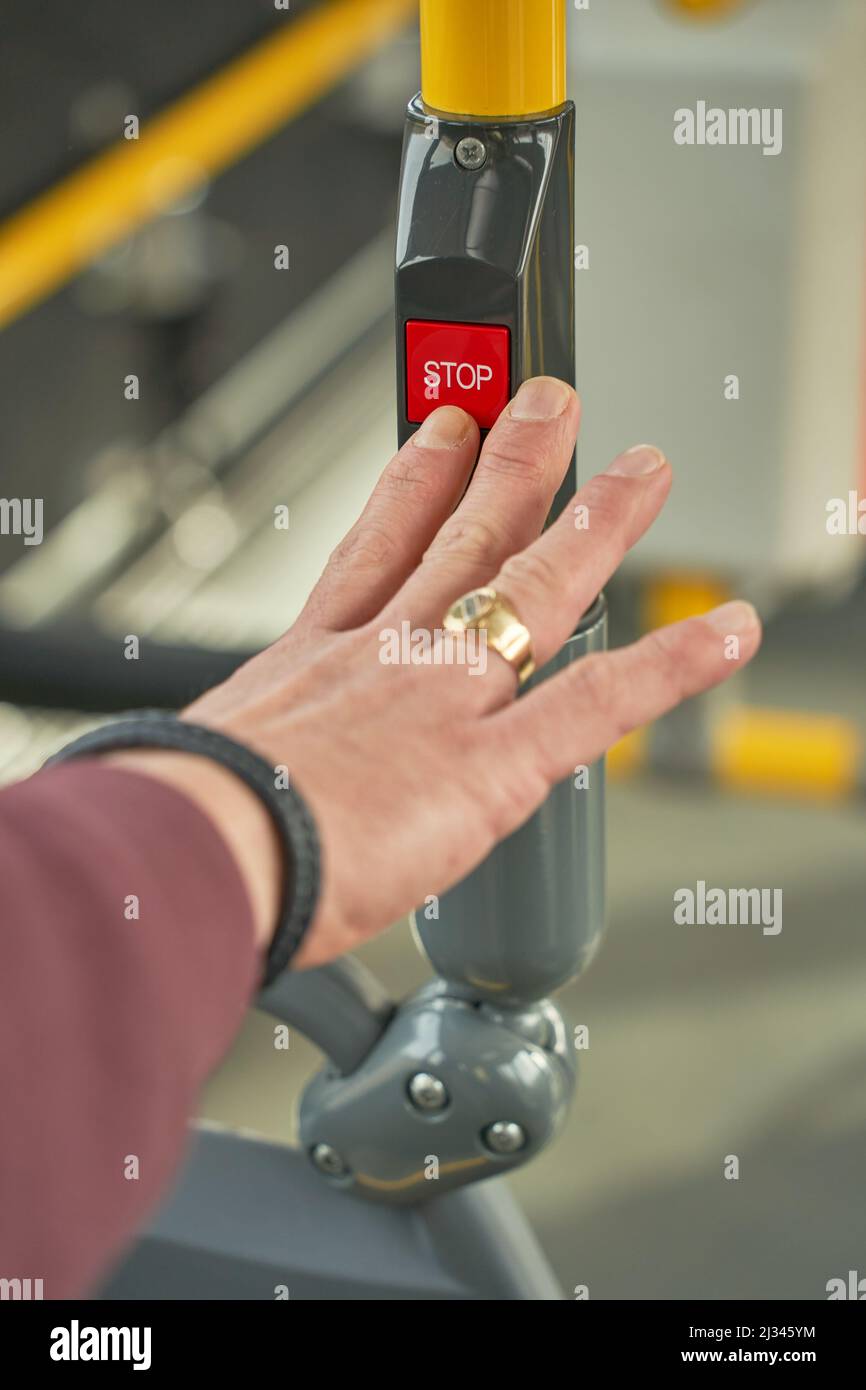 A vertical shot of male hand pushing a bus stop button inside of bus ...