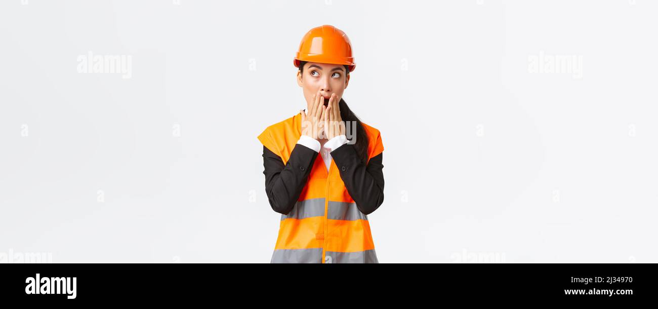 Shocked and concerned asian female engineer, architect in safety helmet ...