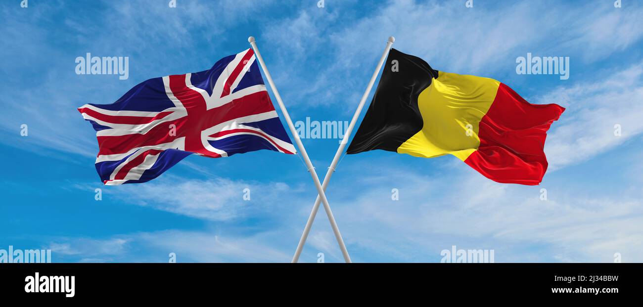 two crossed flags Great Britain and Belgium waving in wind at cloudy ...