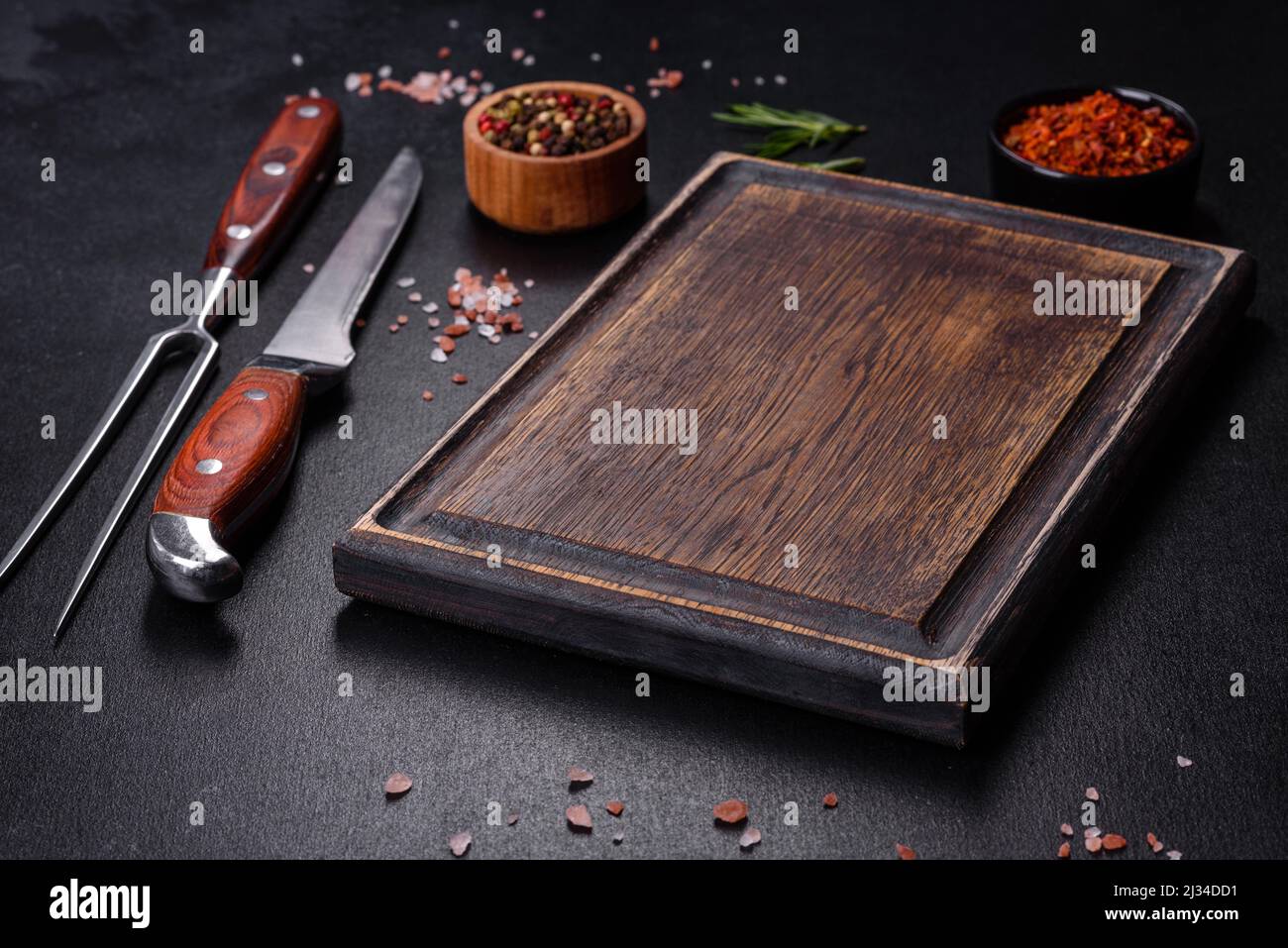 Brown rectangular wooden cutting board with salt and spices on a dark ...