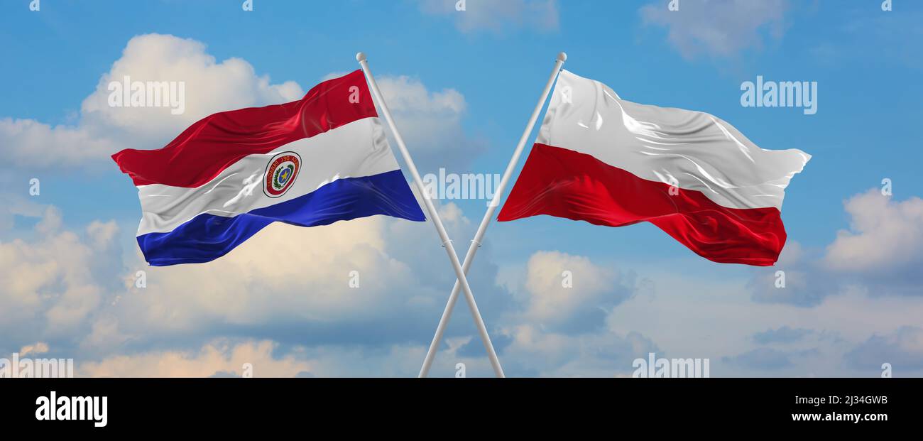 two crossed flags Paraguay and Poland waving in wind at cloudy sky ...