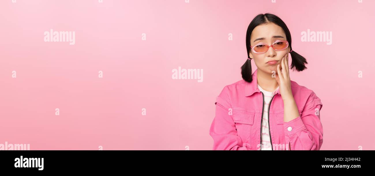 Image of sad asian girl sulking, touching her cheek, pouting ...