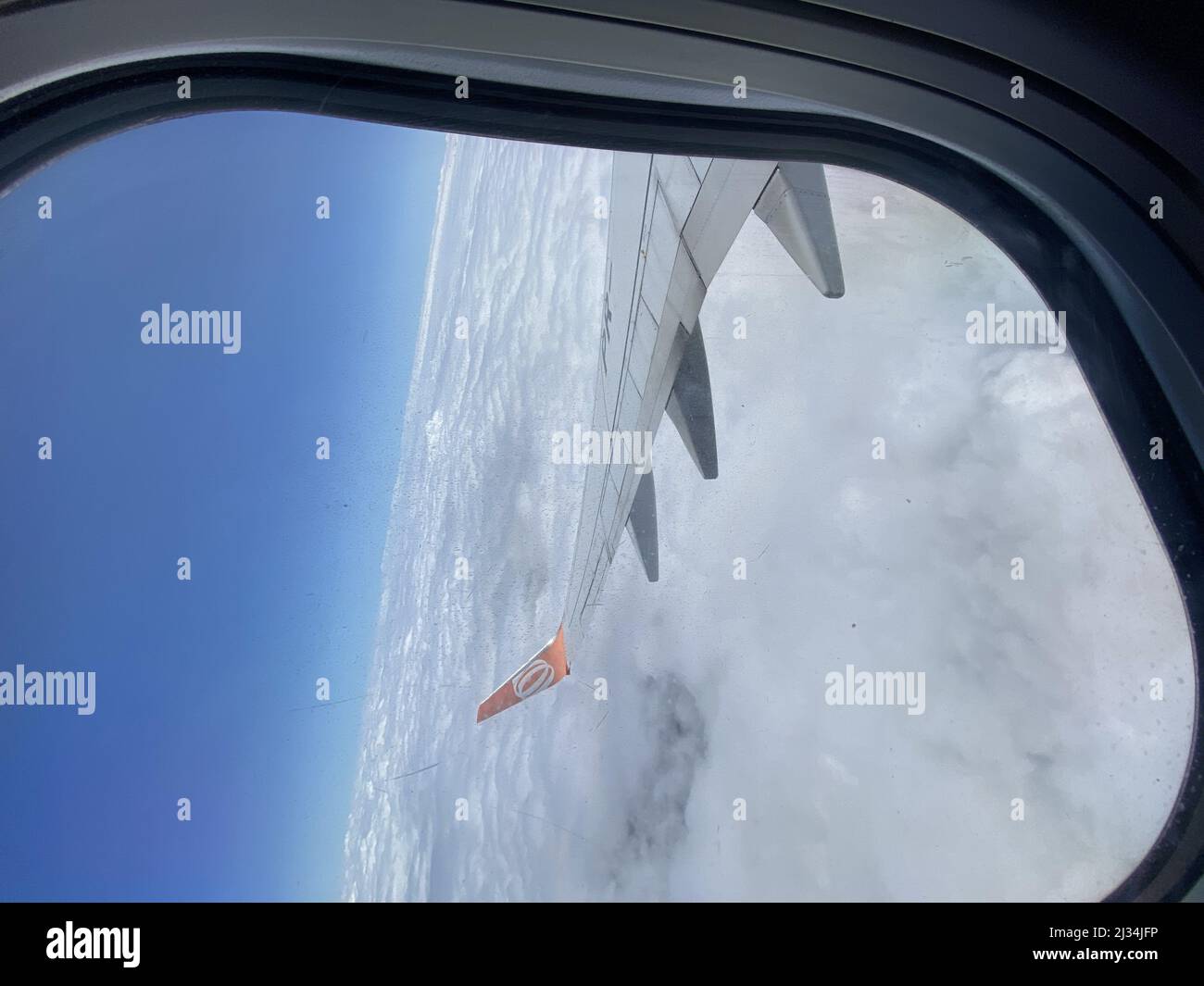 A vertical view of the airplane wing above the clouds behind the window ...