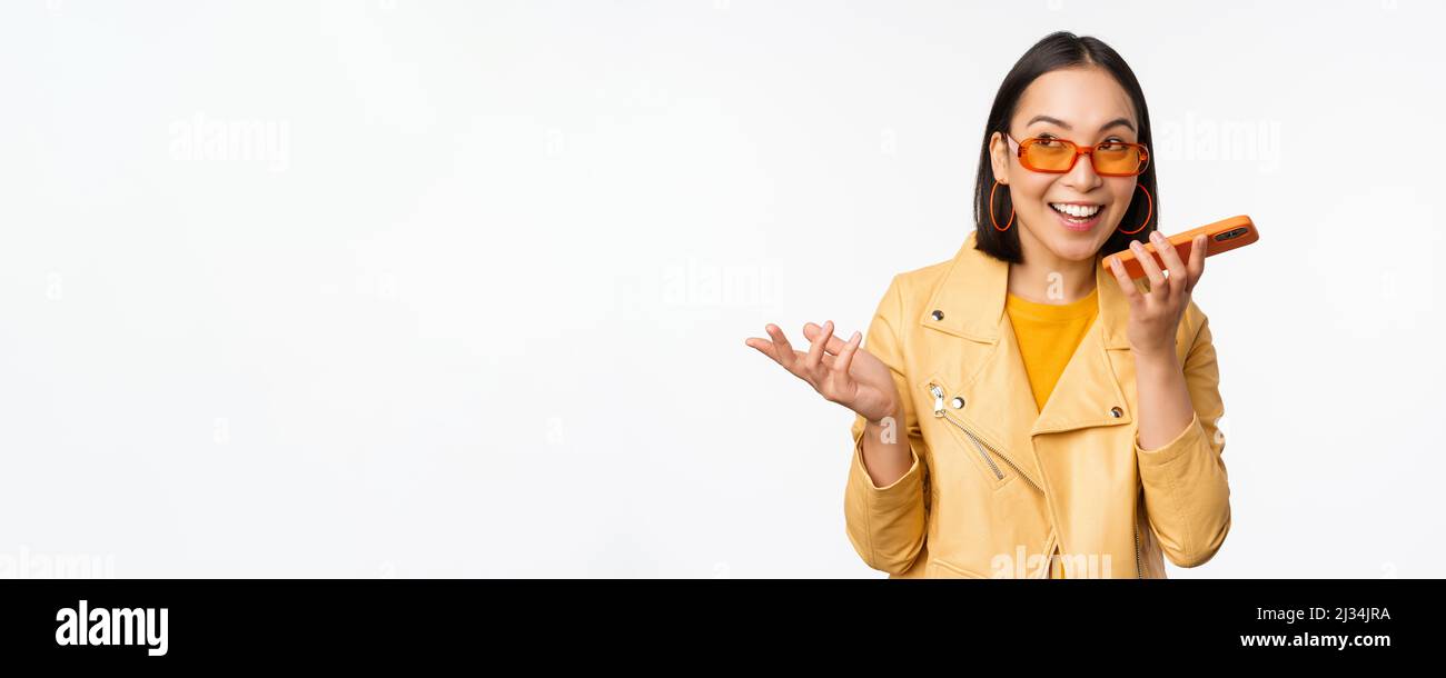 Image of happy asian girl talking on speakerphone, recording ...