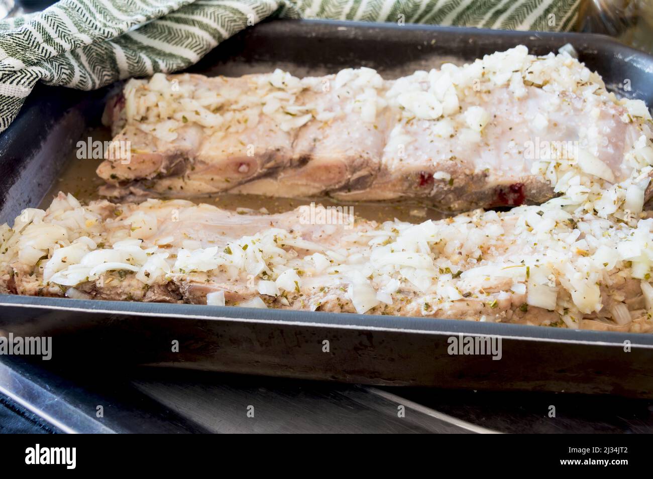 Two beef ribs inside the pan with seasonings over the meat and a ...