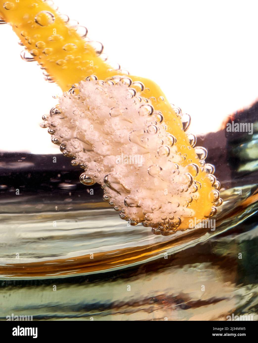 Macro still life of yellow toothbrush in glass showing bubbles formed ...