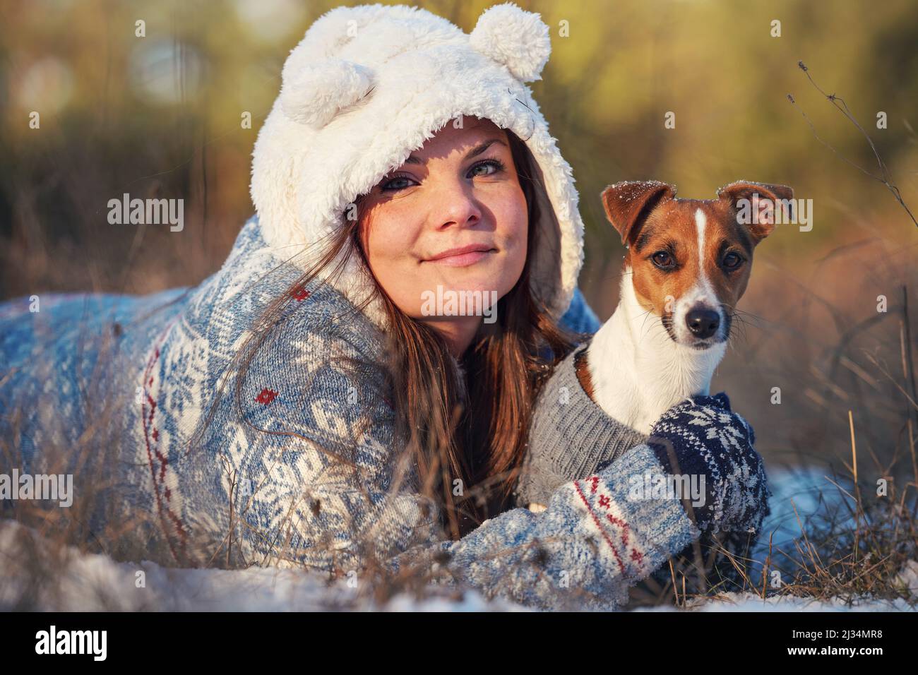Young woman in winter jacket lying down at snow covered ground, holding ...