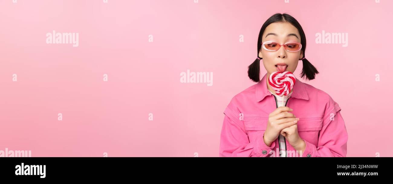 Silly and cute asian female model licking lolipop, eating candy sweet ...