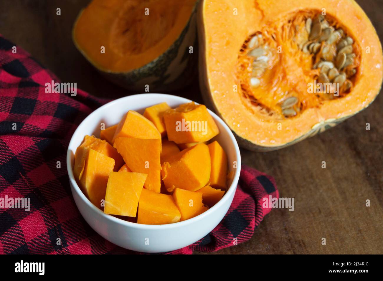Round white bowl with chopped pumpkin on a red checkered cloth and half ...