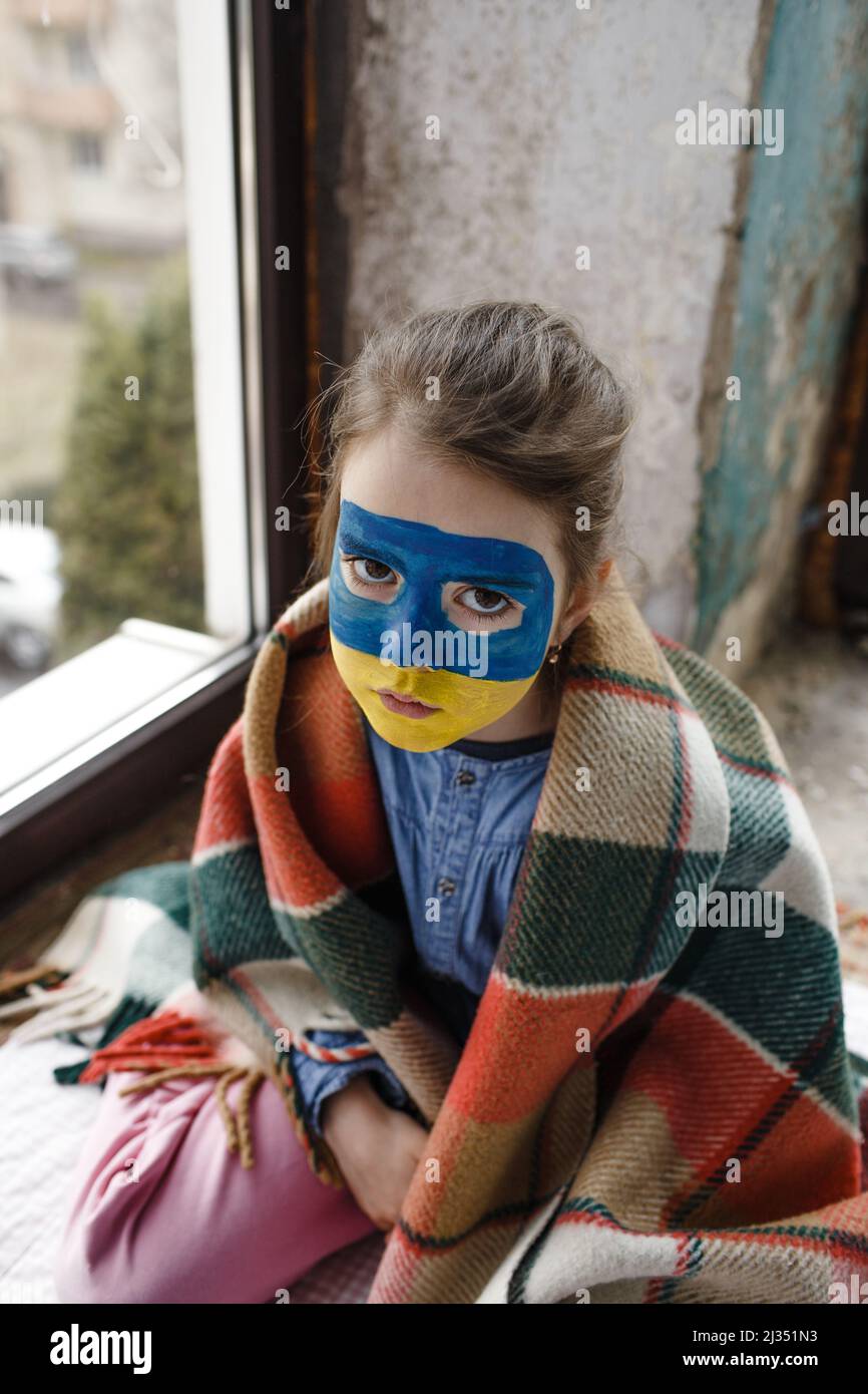 a little girl with a Ukrainian flag painted on her face is sitting ...