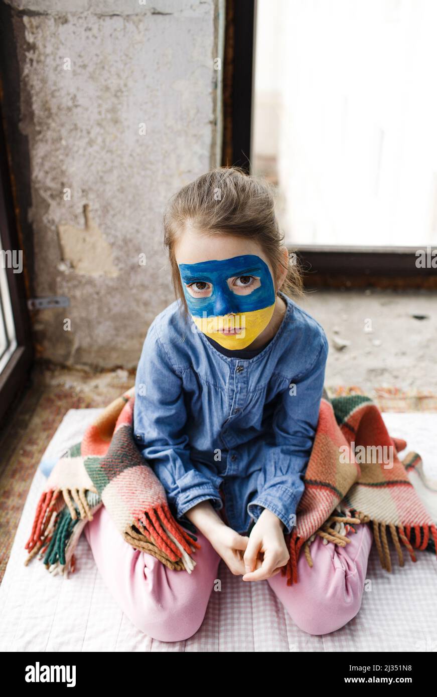 a little girl with a Ukrainian flag painted on her face is sitting ...