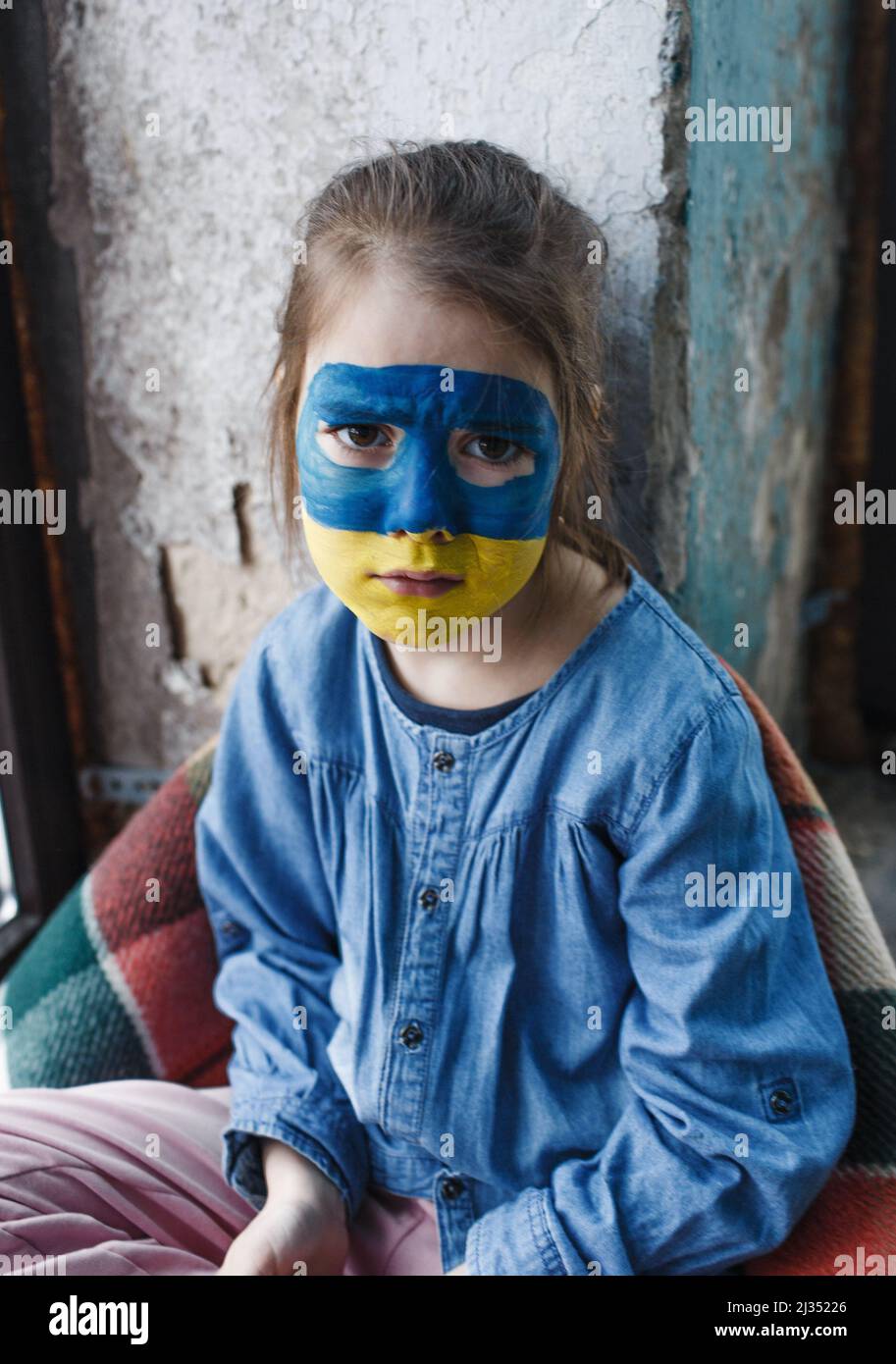 a little girl with a Ukrainian flag painted on her face is sitting ...