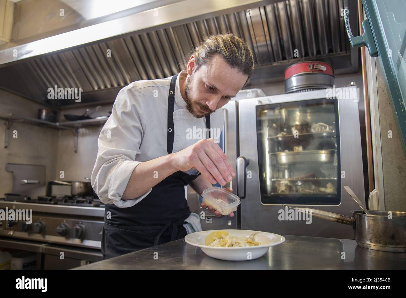 A chef grating cheese making a pancake steak tartare with cheese in a ...
