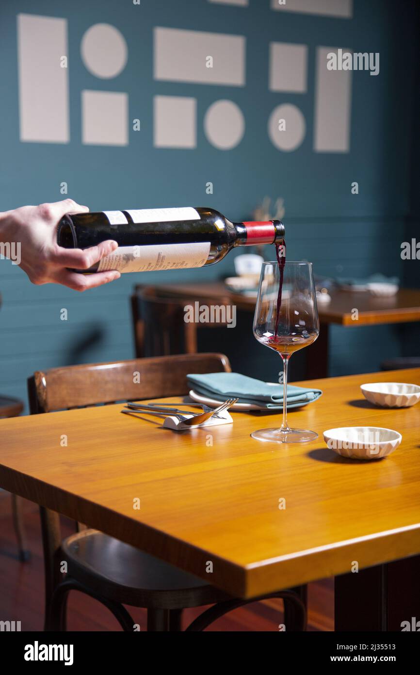 A vertical shot of the hand of a waiter pouring wine into the glass ...