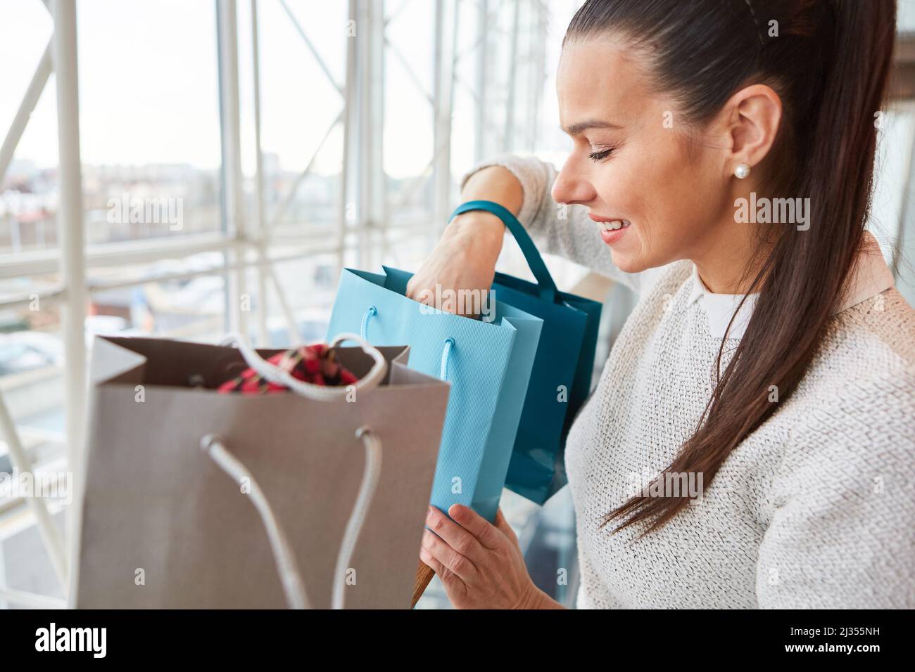 Happy female customer with lots of shopping bags unpacks purchases as ...