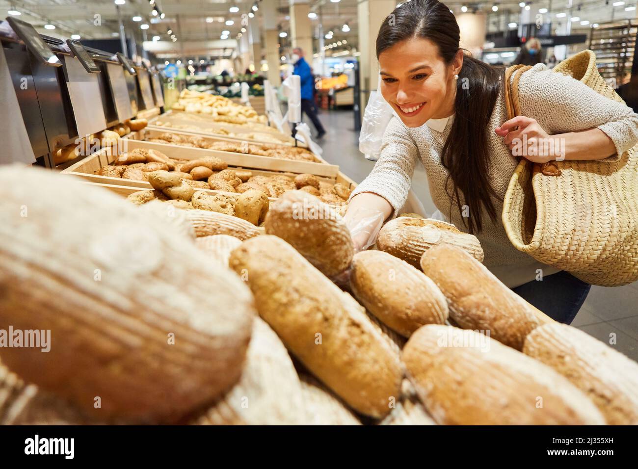 Smiling female customer with shopping bag in front of bread assortment ...