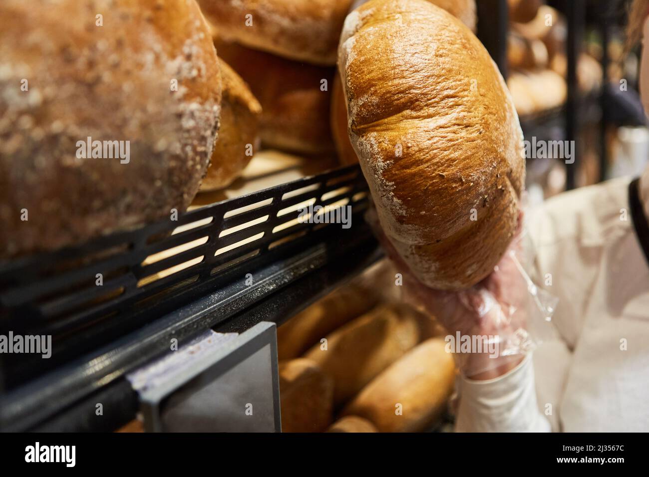Hand takes a loaf of bread from the shelf in the bakery or bakery shop ...