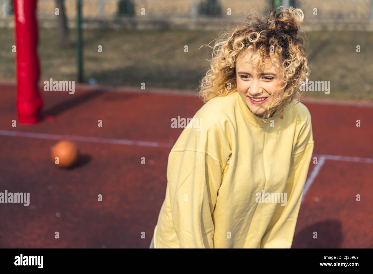 Pretty smiling blond curly haired woman on the sports field, looking ...