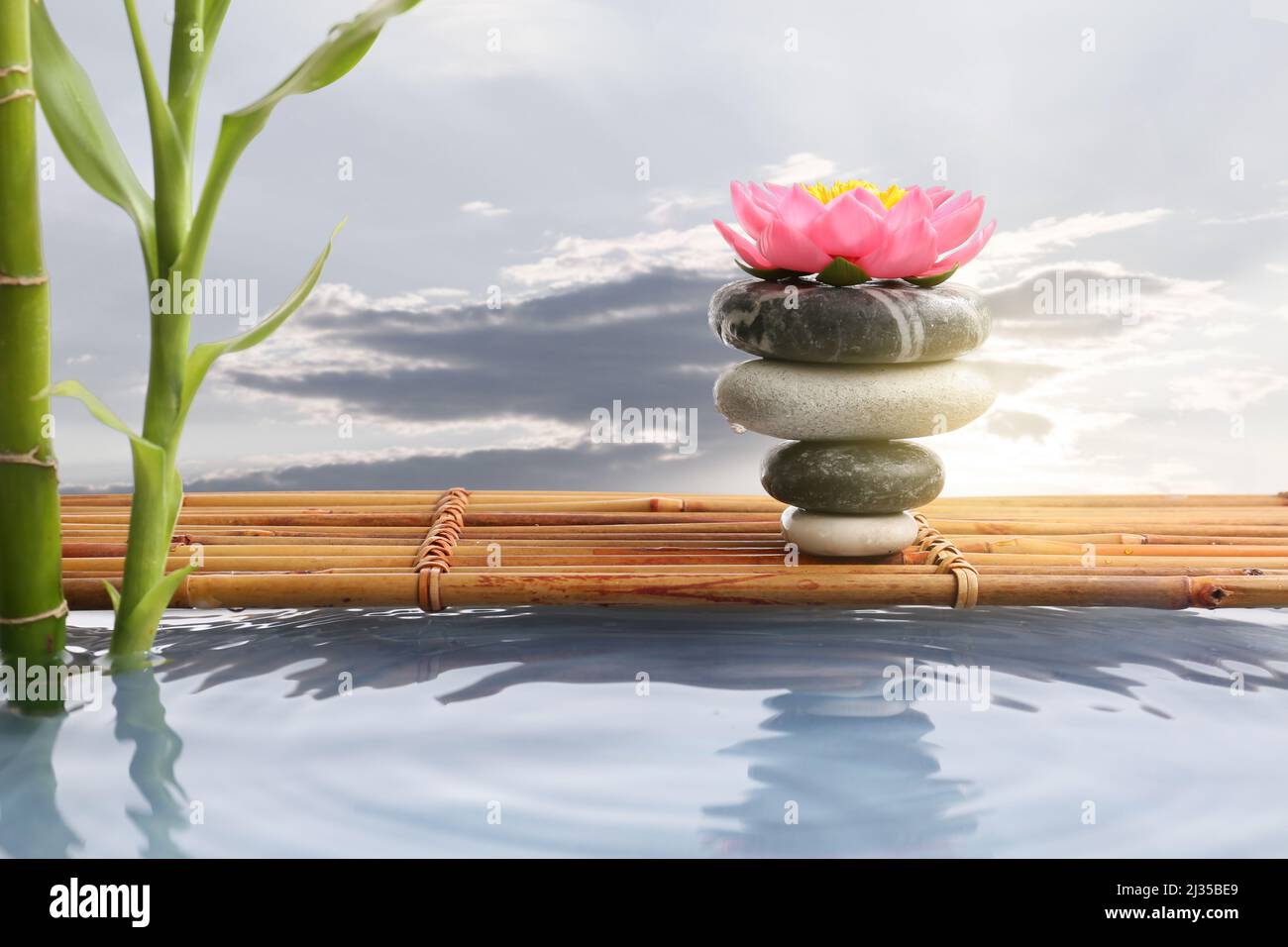 Stack of zen stones with lotus flower, pond and bamboo against cloudy ...