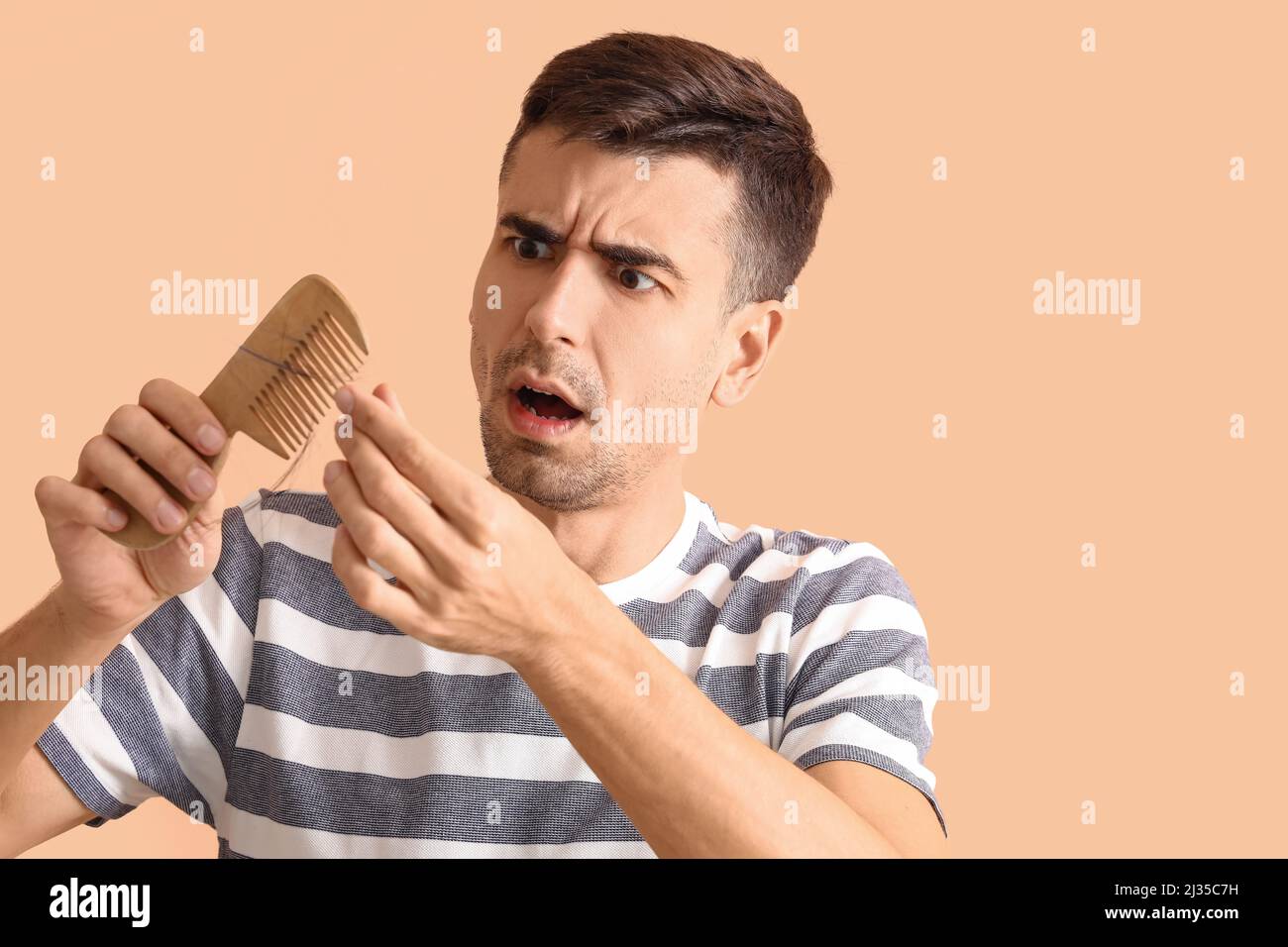 Shocked young man holding comb with fallen down hair on beige ...