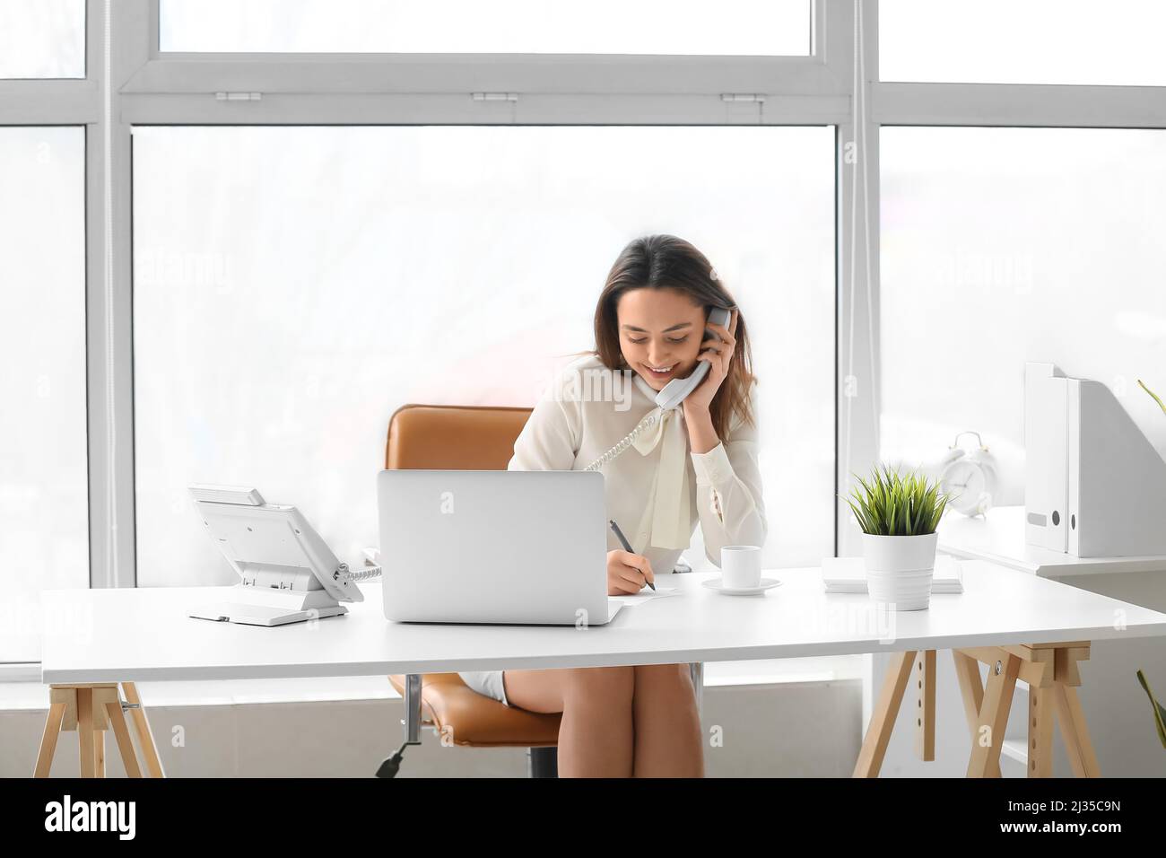 Young secretary talking by phone while working in office Stock Photo ...