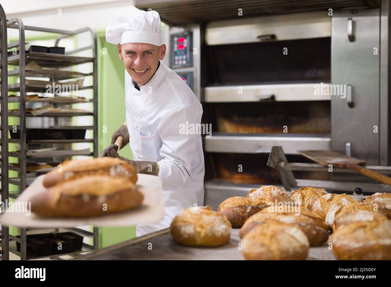 Baker taking out from oven baked bread Stock Photo - Alamy