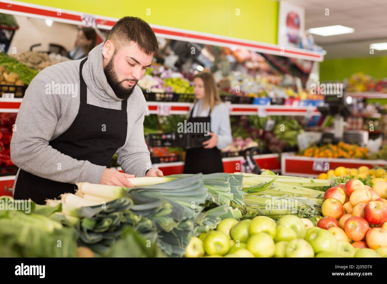 Male shop assistant in apron lays fresh leek in supermarket Stock Photo ...