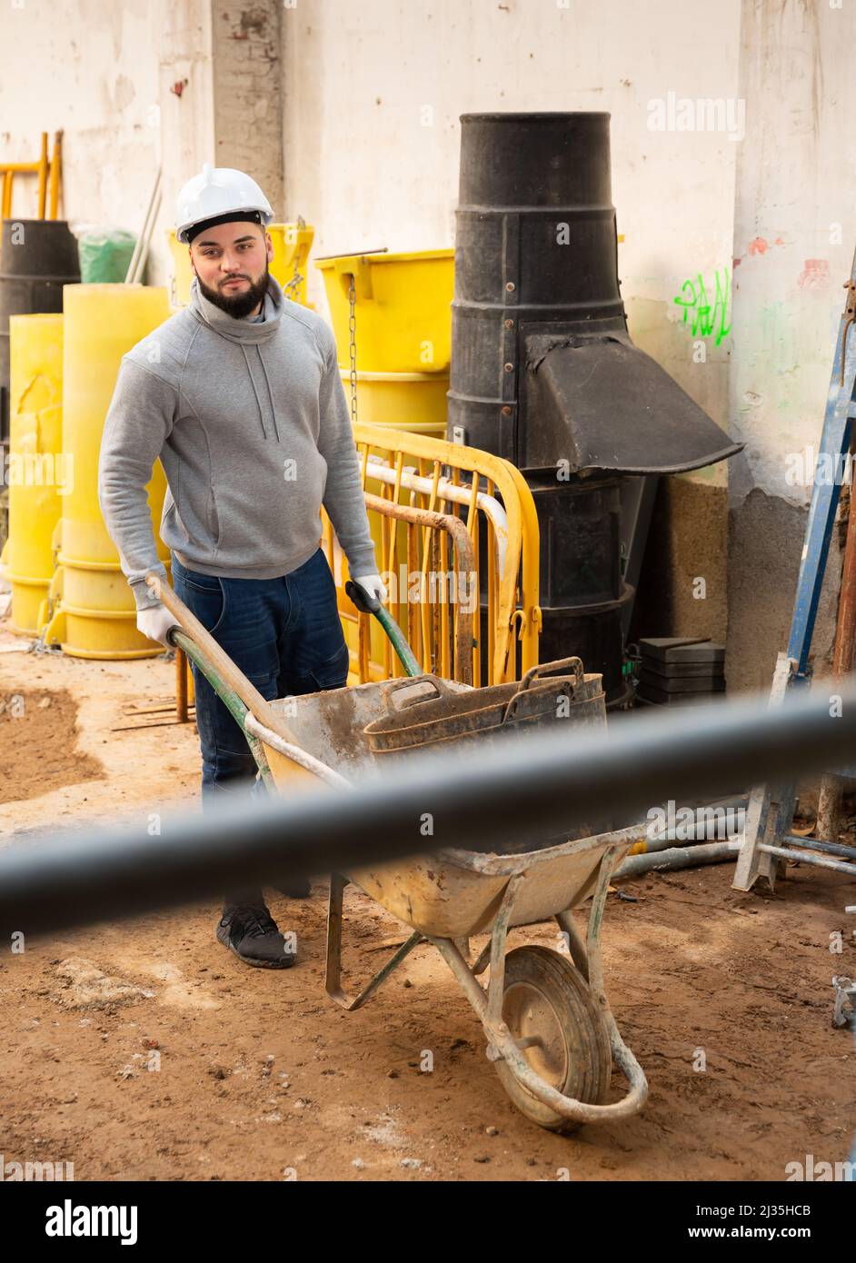 Man carrying wheelbarrow with bucket of mortar Stock Photo - Alamy