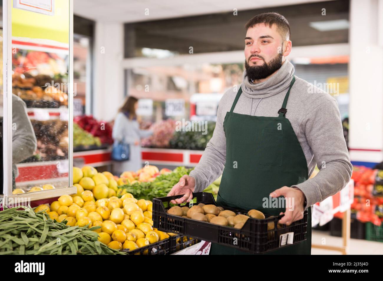 Man seller moving box of kiwi in grocery shop Stock Photo - Alamy
