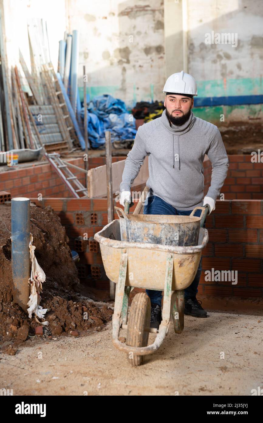 Man carrying wheelbarrow with bucket of mortar Stock Photo - Alamy