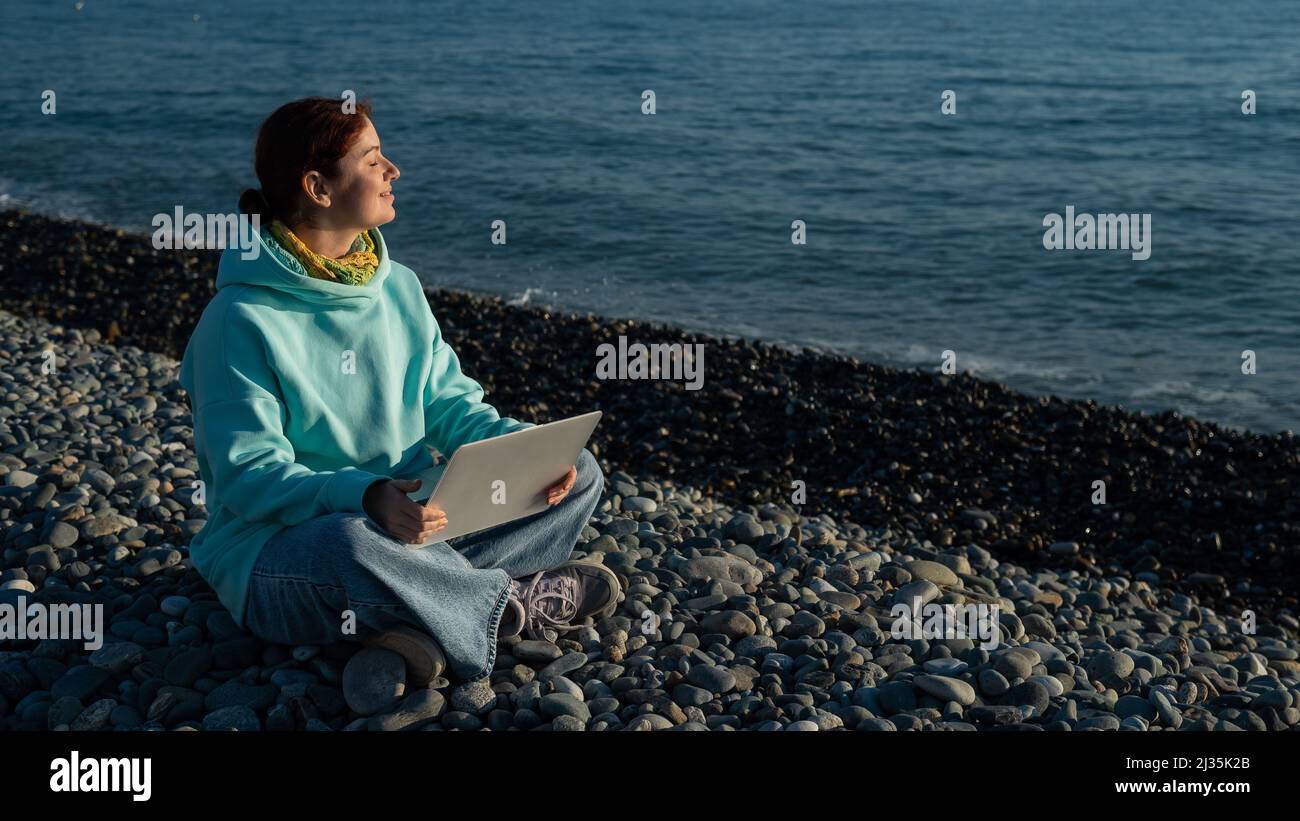 Happy caucasian woman working on a laptop while sitting on a pebble ...