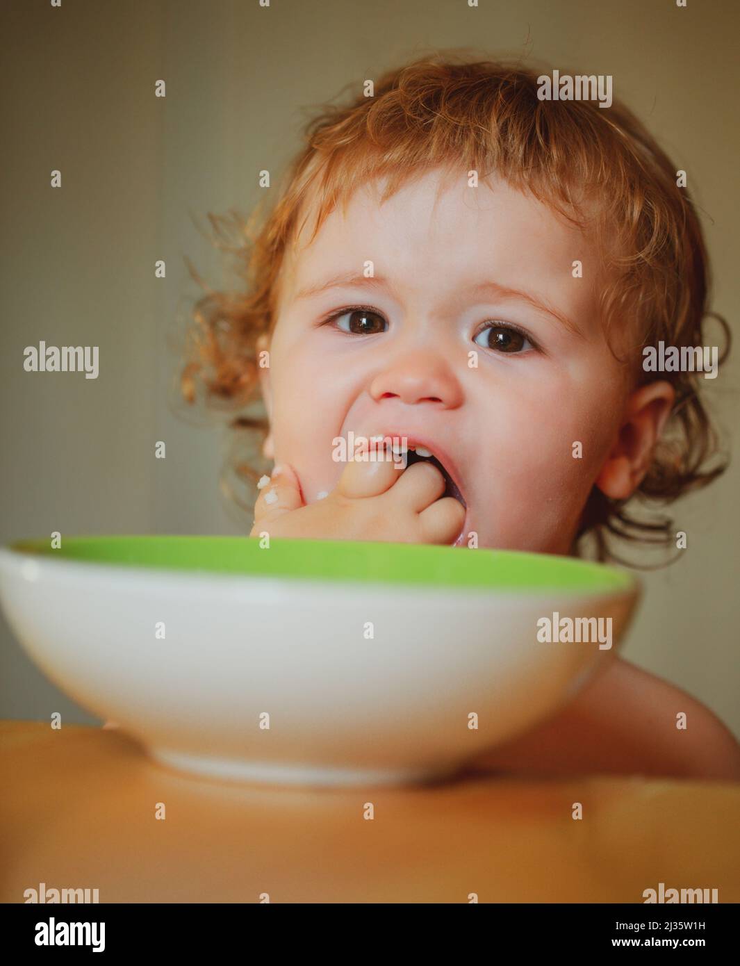 Portrait of funny little baby boy eating from plate holding spoon ...