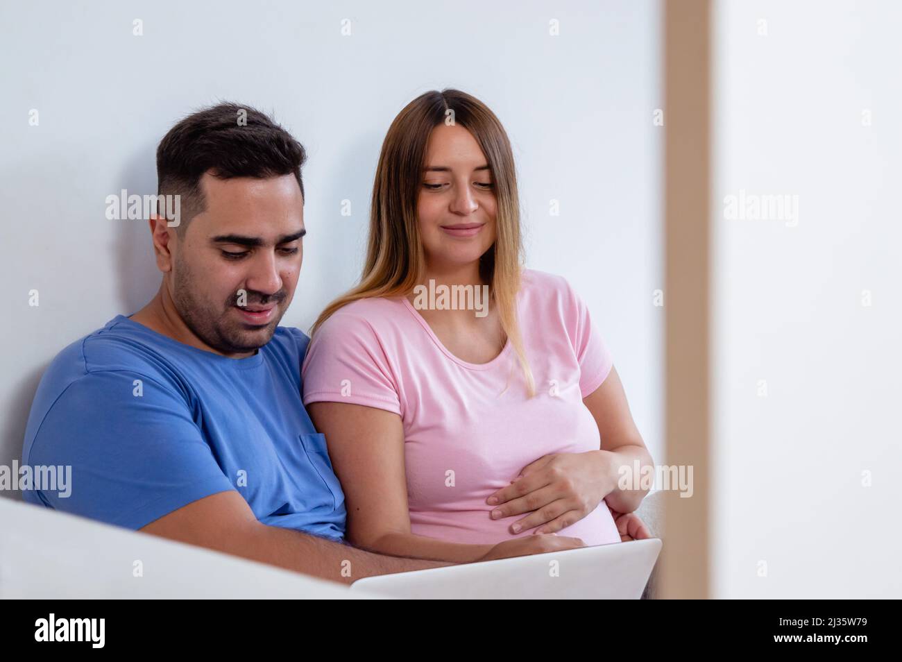 Side View Young Venezuelan Man Sitting With His Pregnant Wife In The Room In Pajamas Sitting On