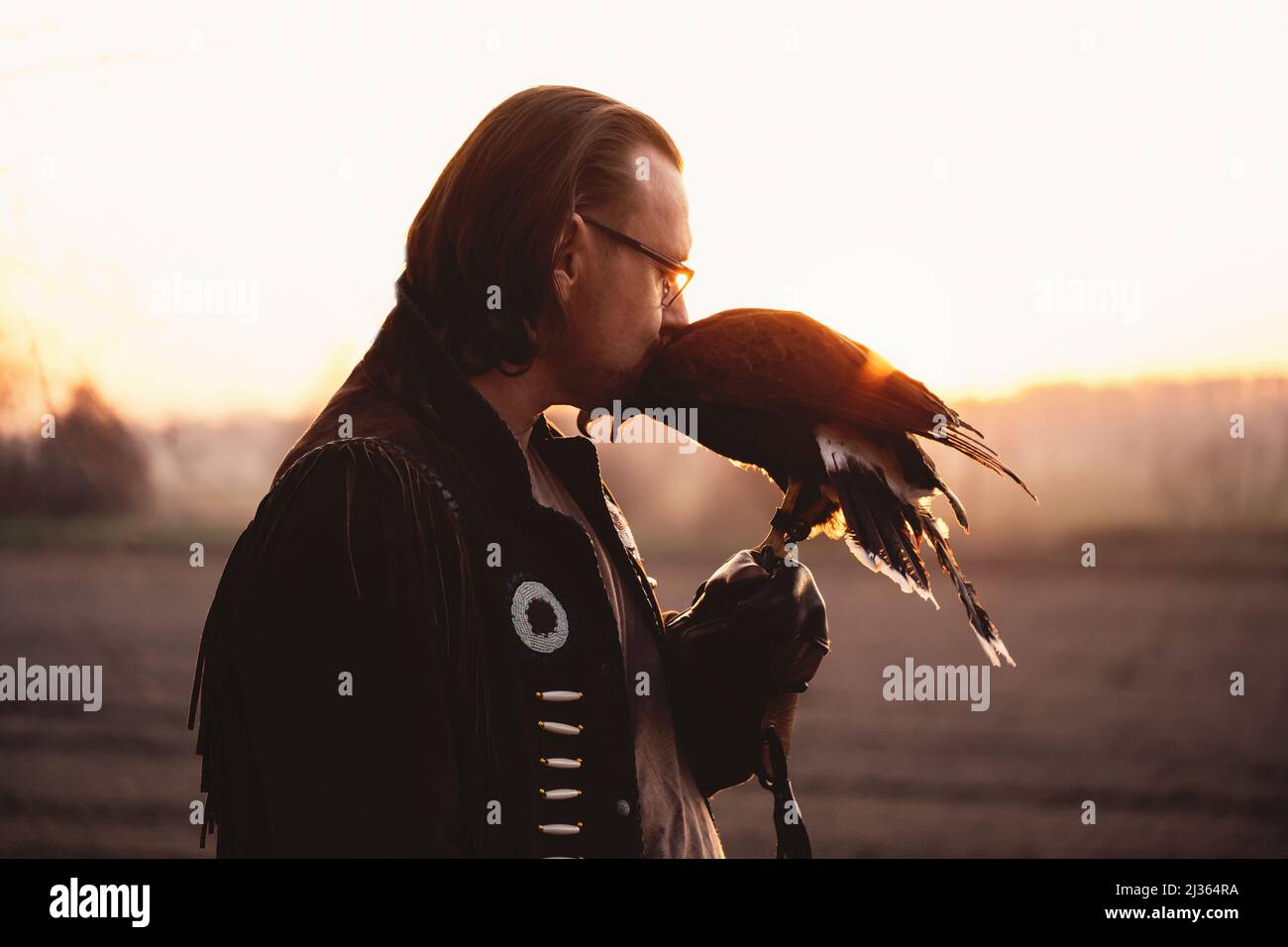 Man and wild bird over sunset sky looking on each other Buzzard or ...