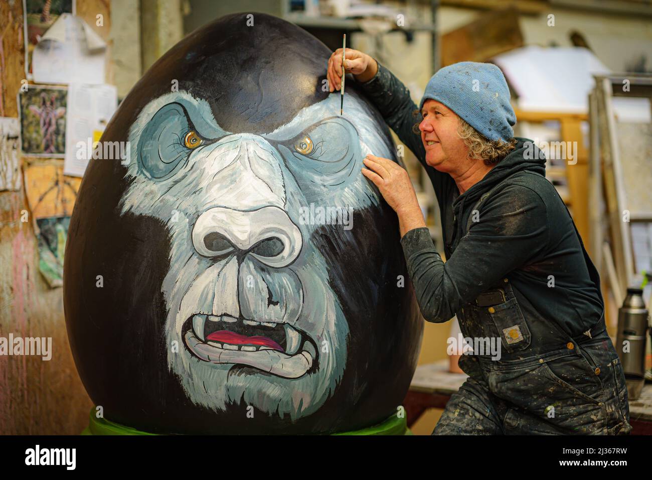 Sculptor Bruce Hansing paints a gorilla face on a Easter egg, one of ...
