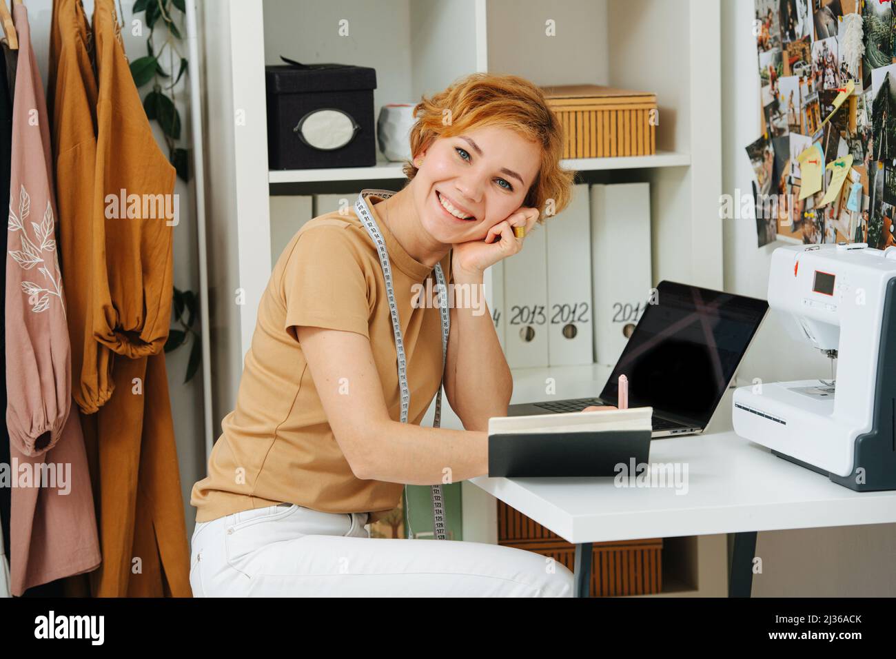 Radiantly smiling seamstress sitting behind her workdesk, writing in a ...