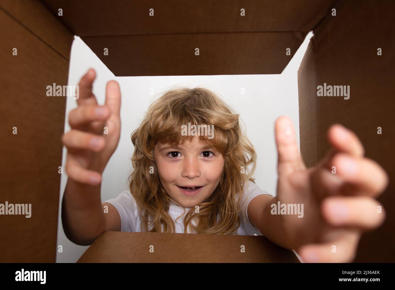 Child opens carton box and pulling out gift from it. Small boy looking ...