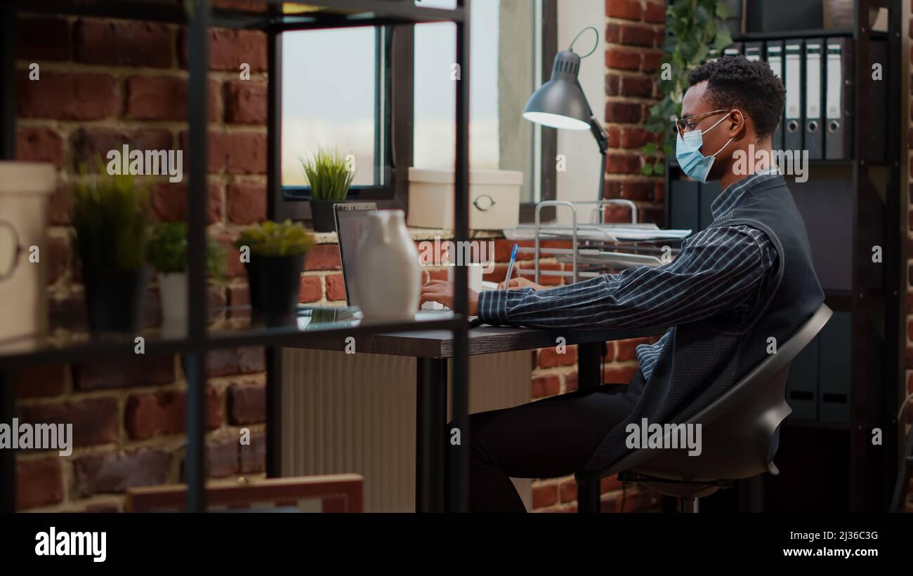 Accountant with face mask planning marketing project on laptop at ...