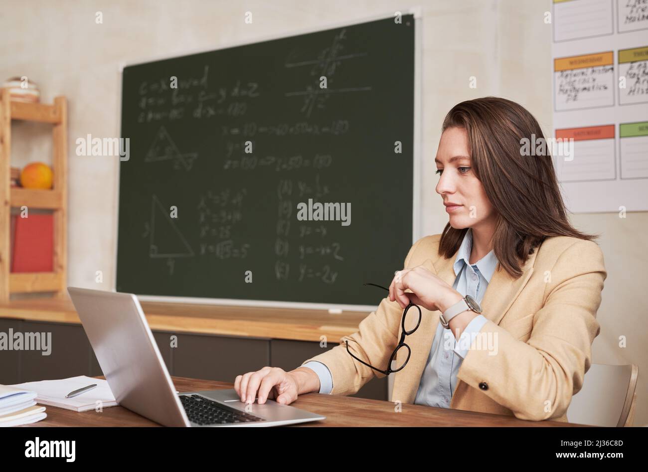 Side view portrait of young female teacher sitting at desk in school ...