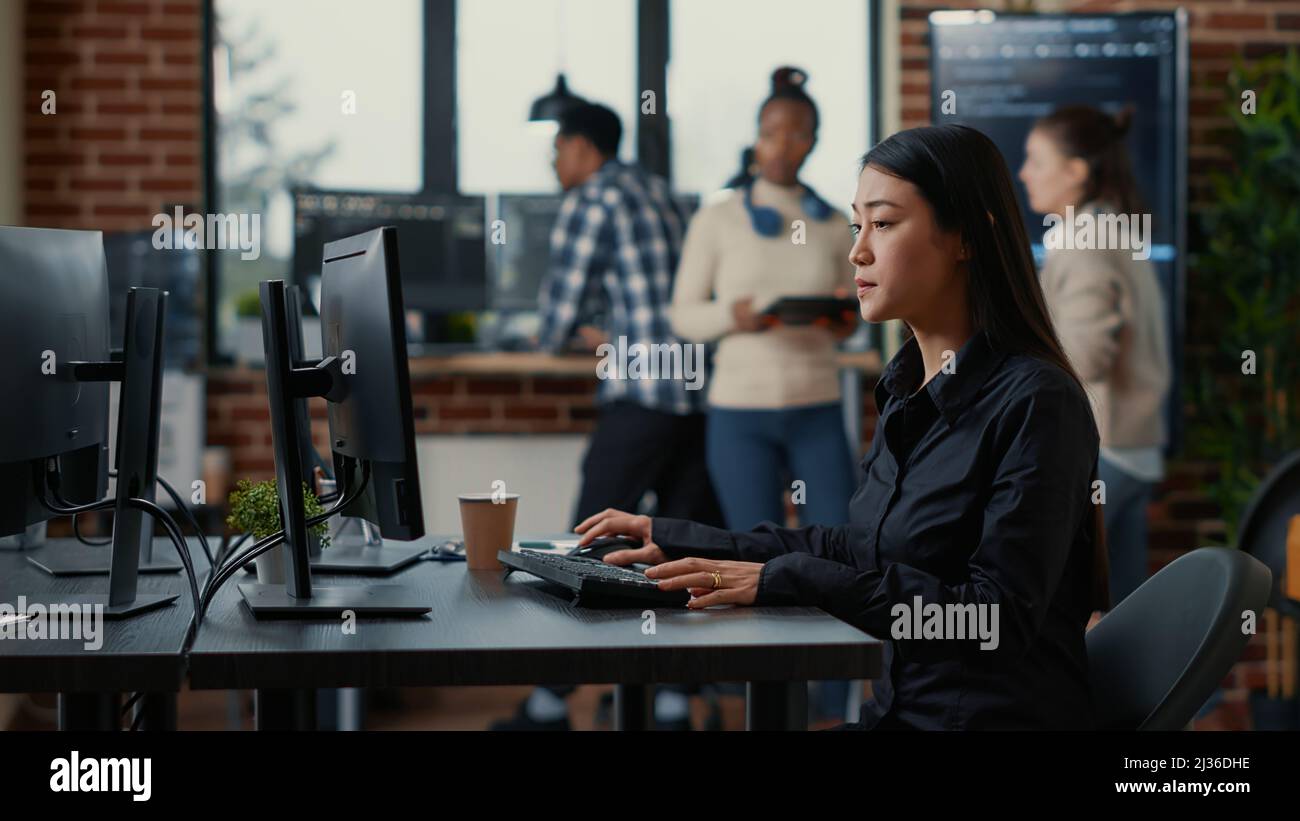 Asian software developer holding clipboard sitting down and starting to type on computer ...
