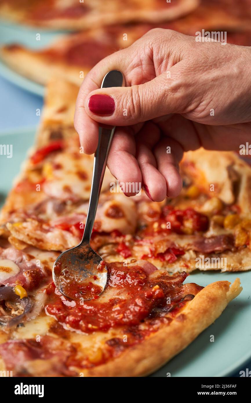 Woman's hand spreading hot sauce on a pizza slices, closeup Stock Photo ...