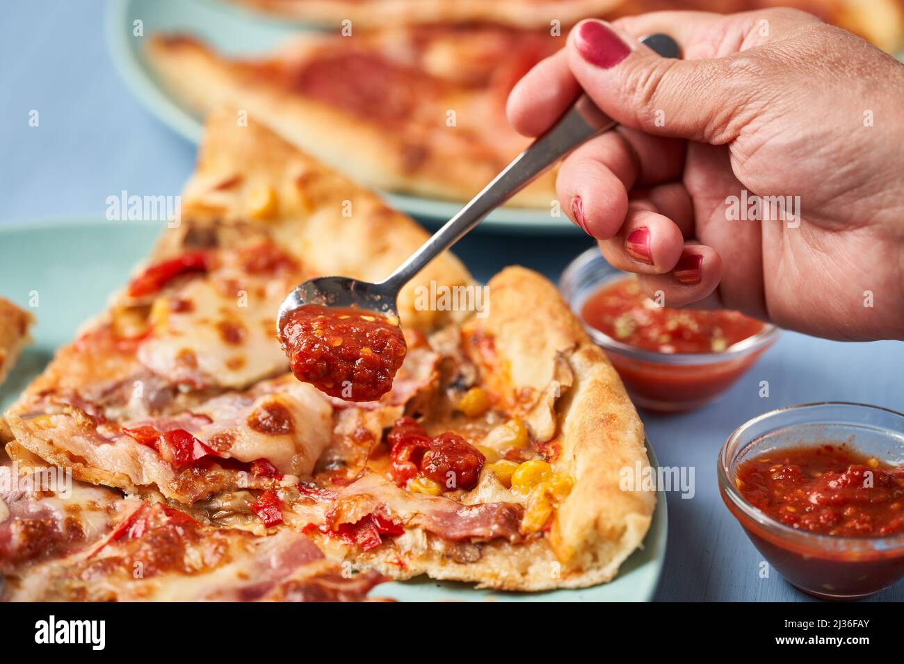 Woman's hand spreading hot sauce on a pizza slices, closeup Stock Photo ...