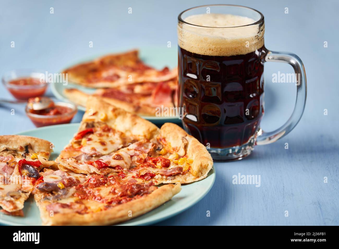 Dark beer in a mug and pizza slices on blue background Stock Photo - Alamy