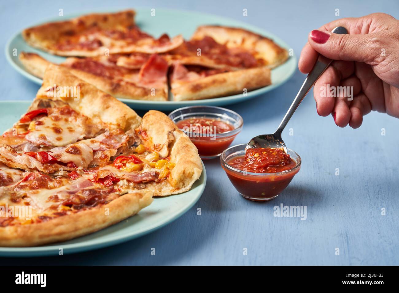 Woman's hand spreading hot sauce on a pizza slices, closeup Stock Photo ...