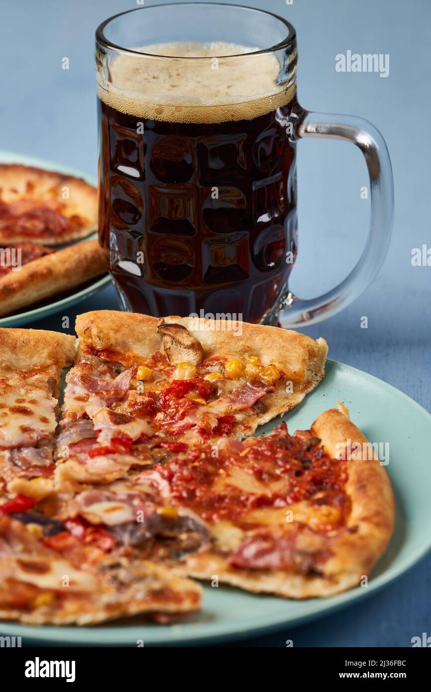 Dark beer in a mug and pizza slices on blue background Stock Photo - Alamy