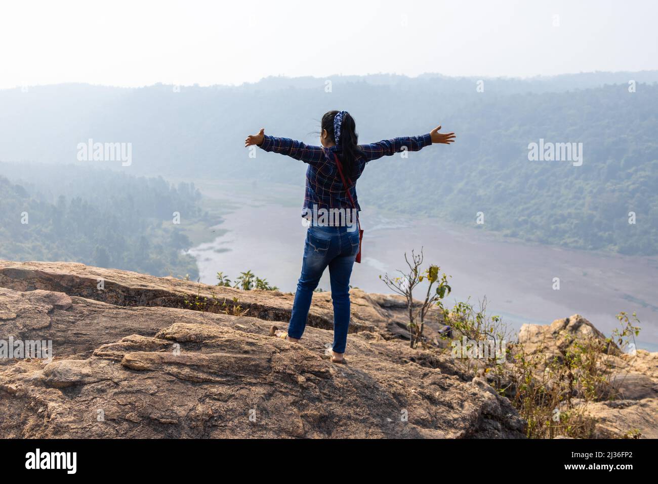 An woman with outstretched hands standing on hill top facing backside ...