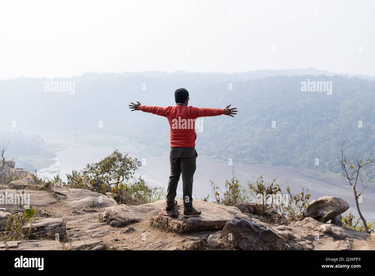 A man with outstretched hands standing on hill top facing backside and ...