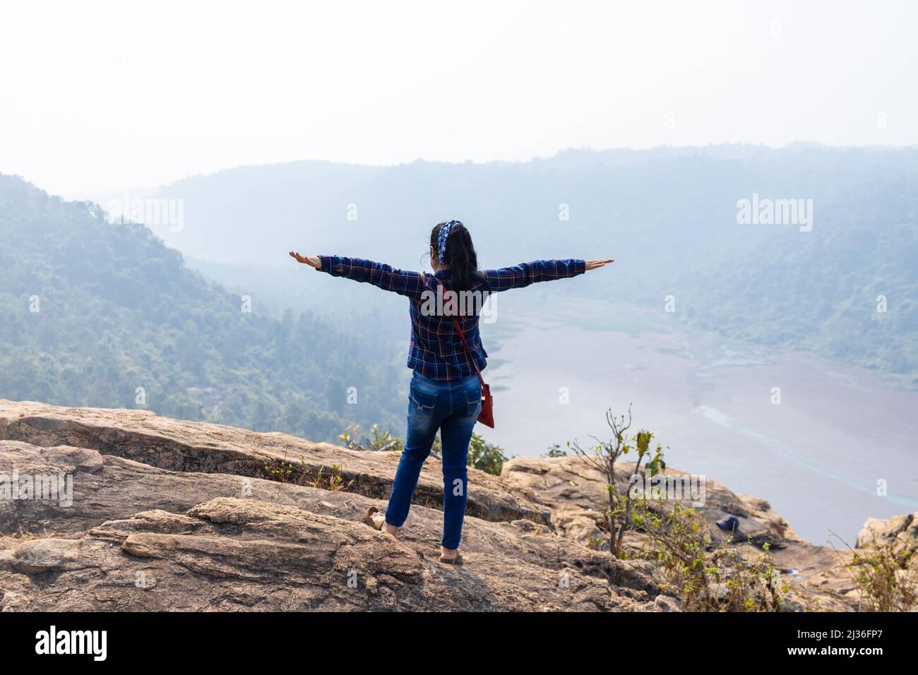 An woman with outstretched hands standing on hill top facing backside ...